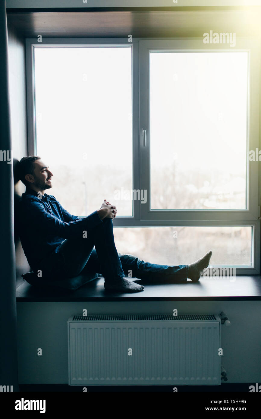 Handsome young man sitting on windowsill Stock Photo - Alamy