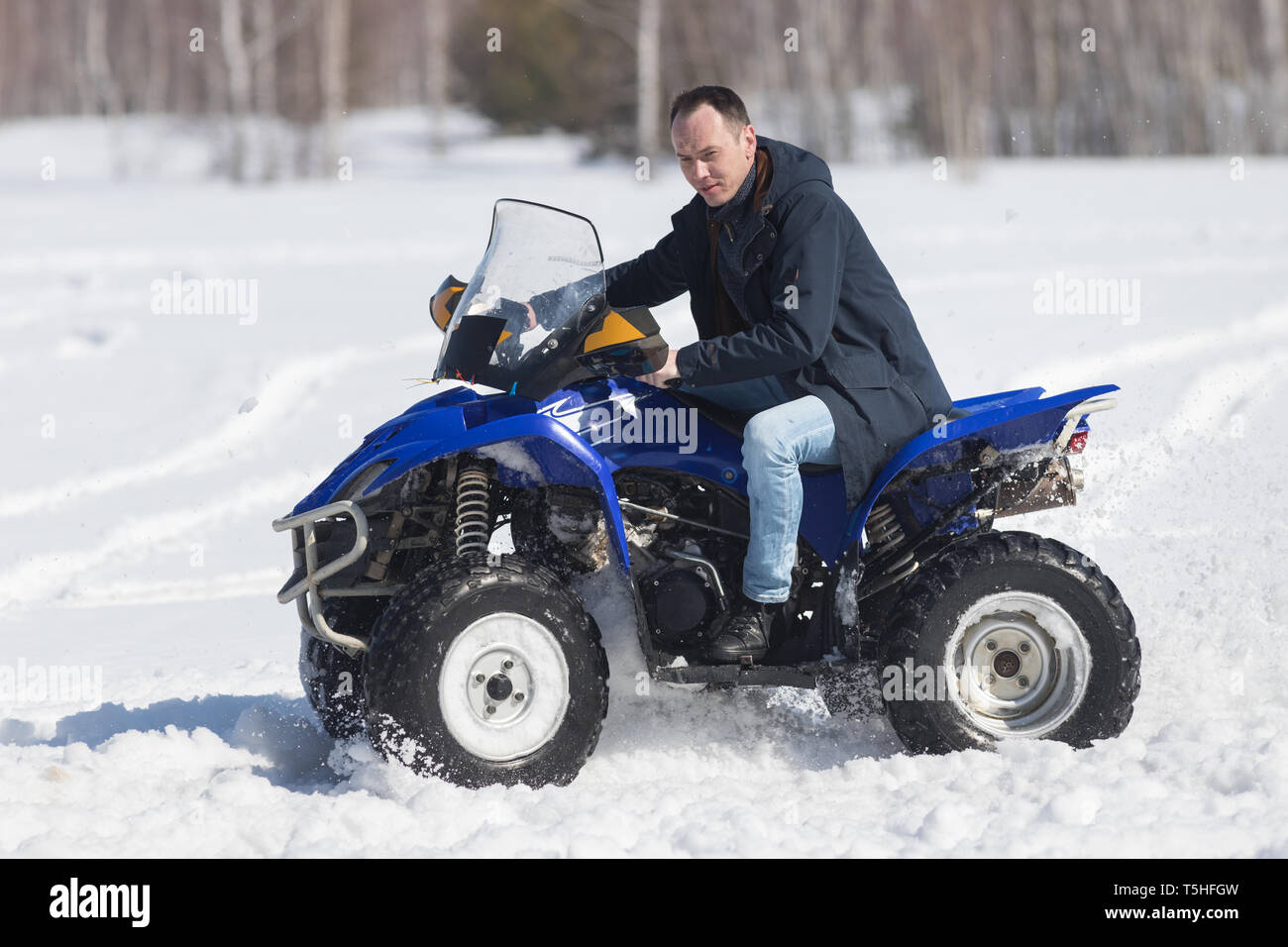 A winter forest in daylight. A man riding a big blue snowmobile. Side ...