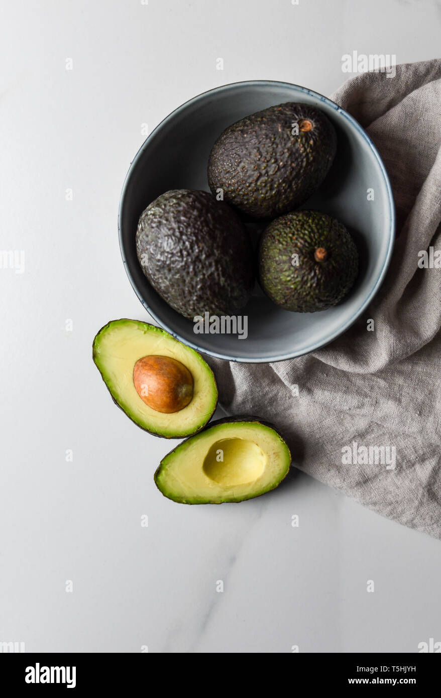 Bowl of avocados with one cut in half on a white countertop Stock Photo ...
