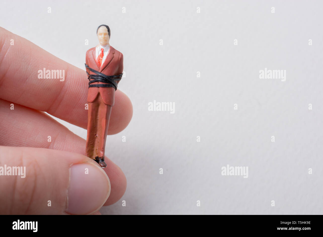 Hand holding tiny figurine of man model tied in a rope Stock Photo - Alamy