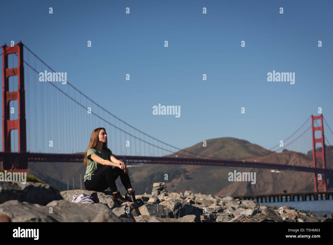 Beautiful woman sitting on rock near golden gate bridge Stock Photo - Alamy