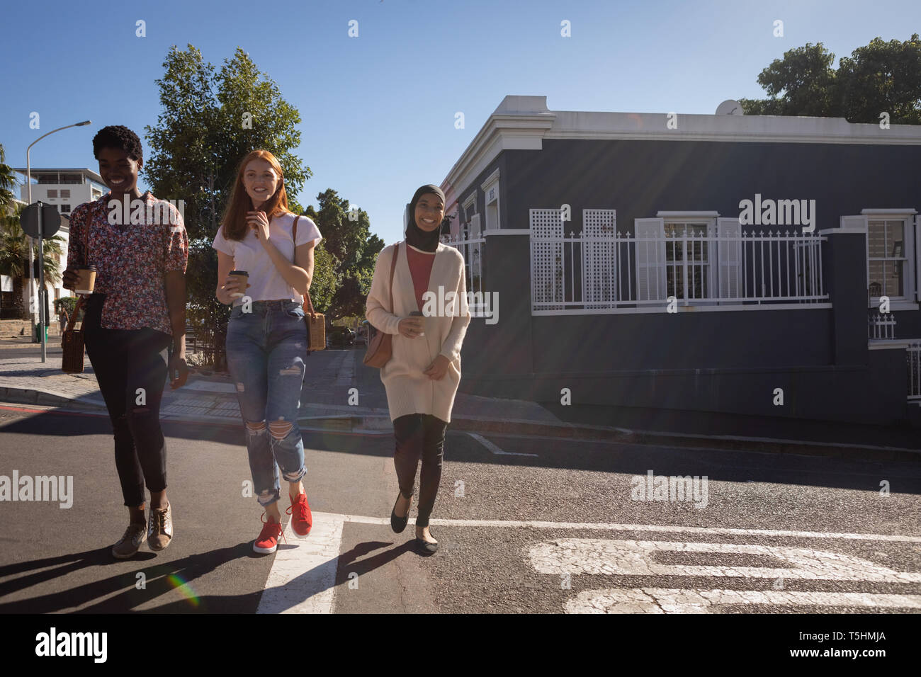 Female friends interacting with each other while crossing the road ...
