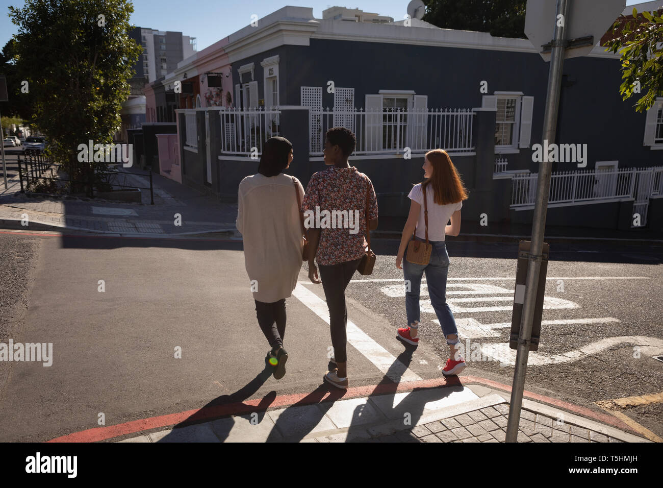 Female friends interacting with each other while crossing the road ...