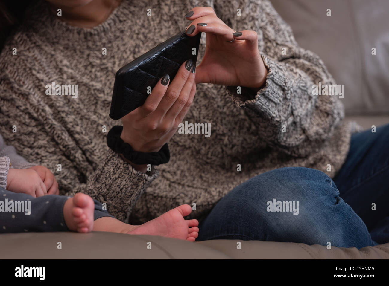 Mother and daughter using mobile phone while sitting on sofa Stock ...