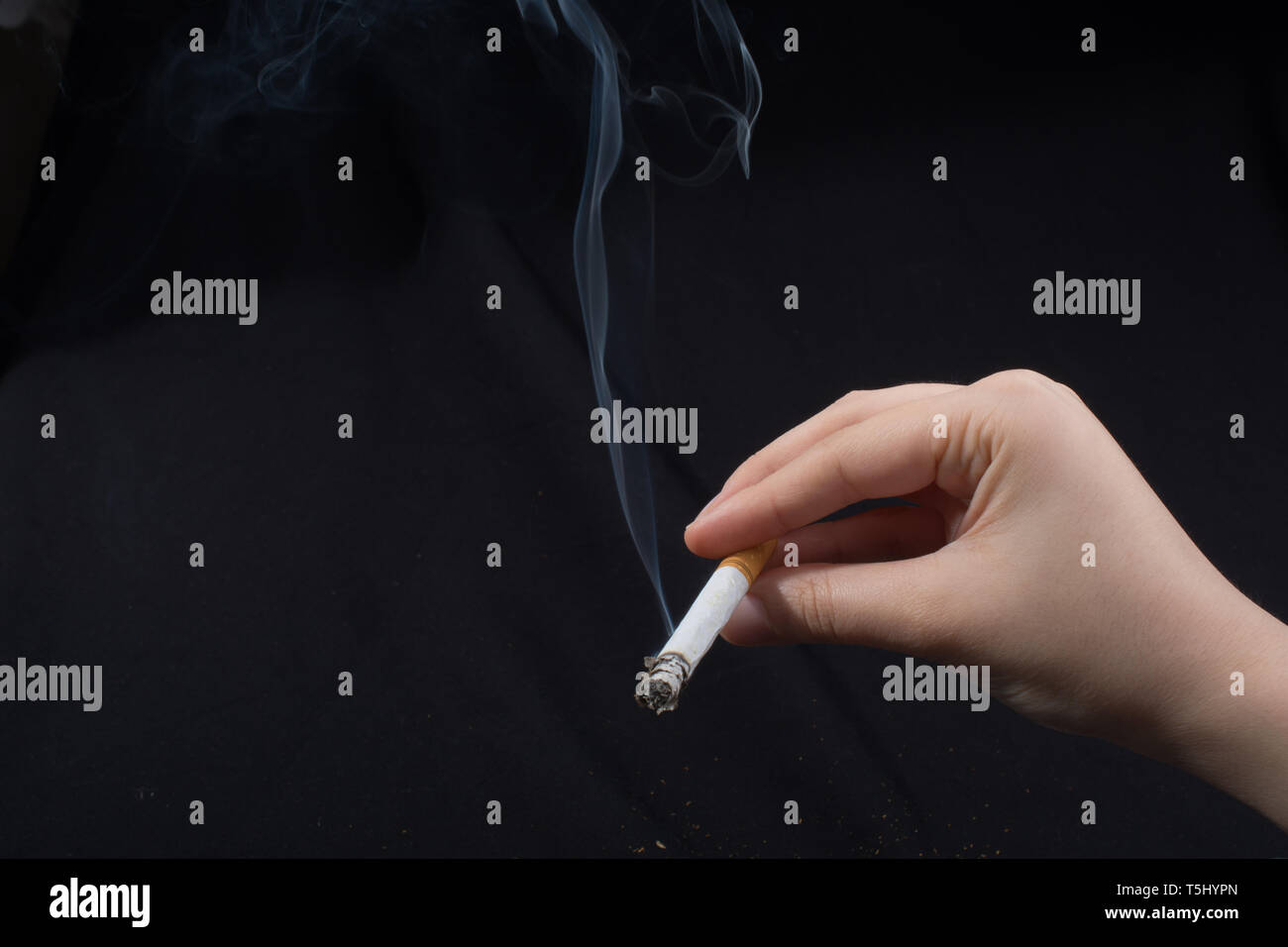 Hand is holding smoking cigarette with smoke around Stock Photo - Alamy