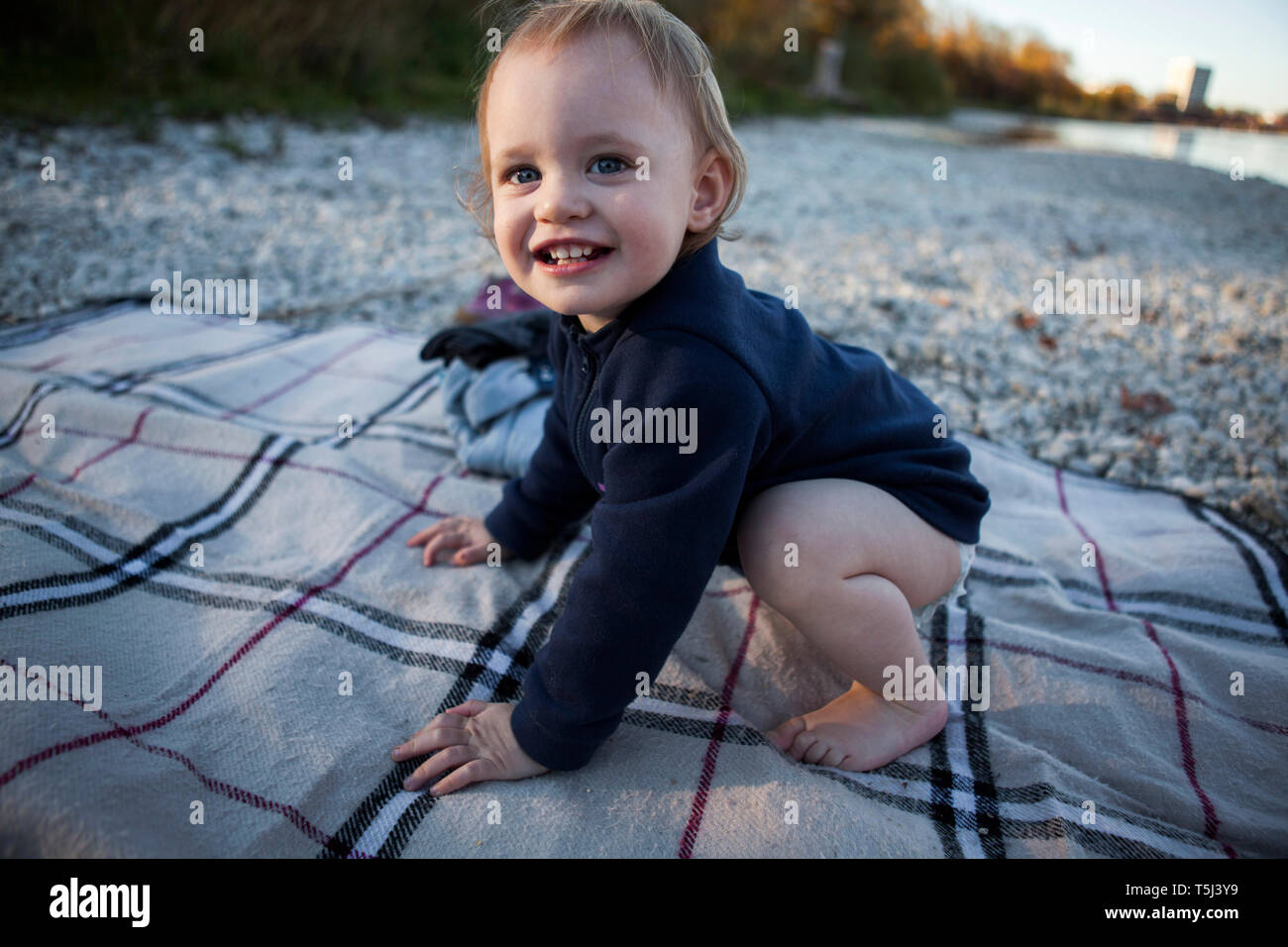 Portrait of smiling toddler girl crouching barefoot on blanket on the ...