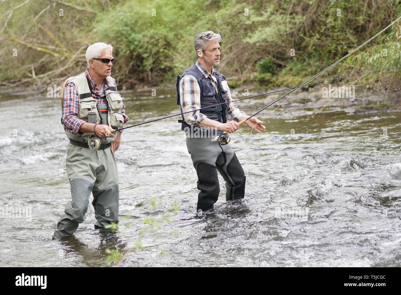 Fly fishing expert guiding novice in river Stock Photo - Alamy