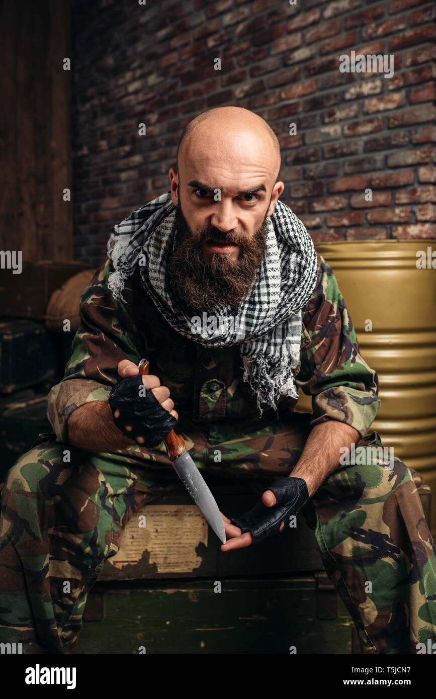 Terrorist in uniform with knife in hands sitting on boxes of ammunition ...