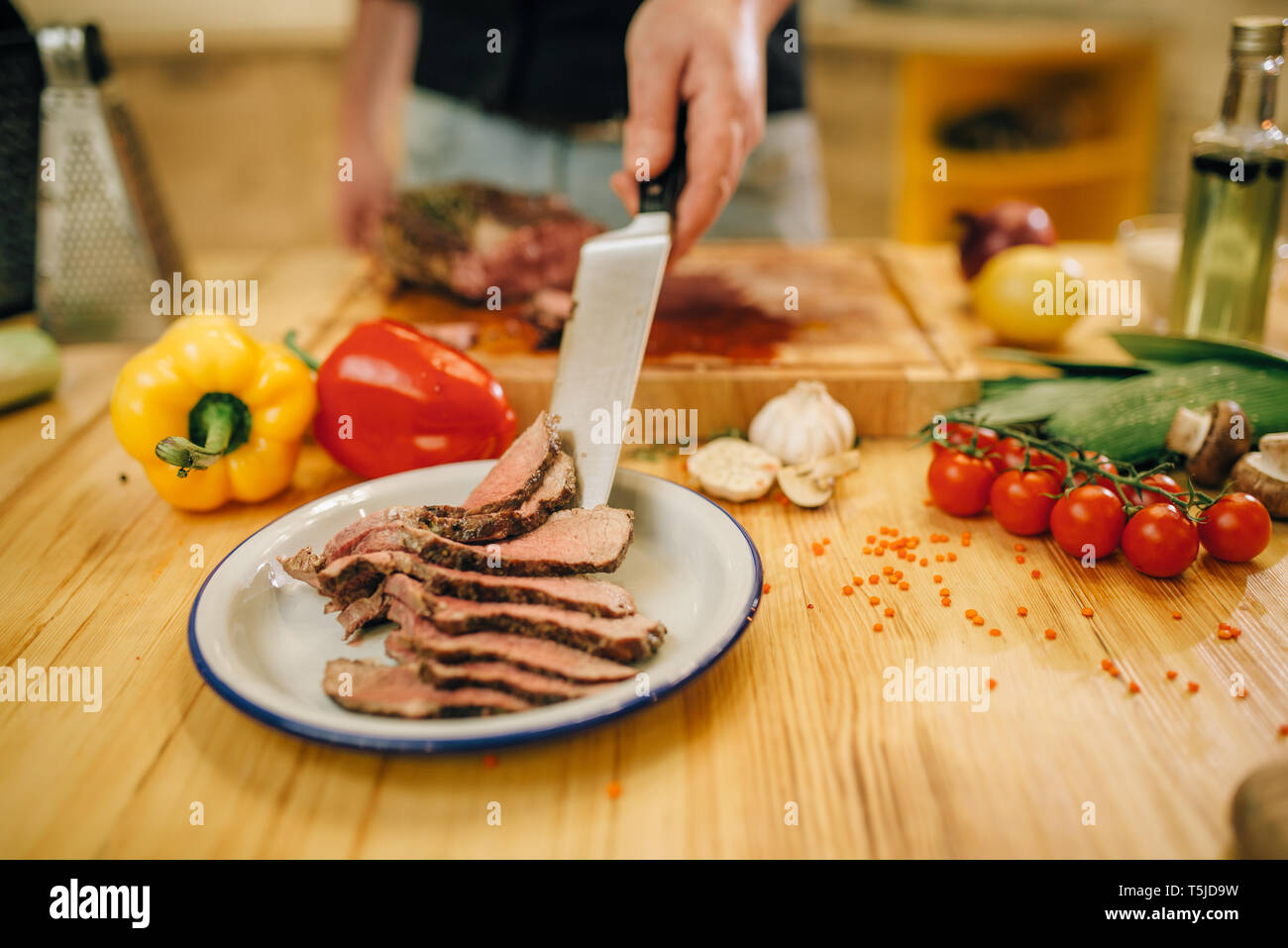 Male chef with knife puts roasted meat slices into the plate, kitchen ...