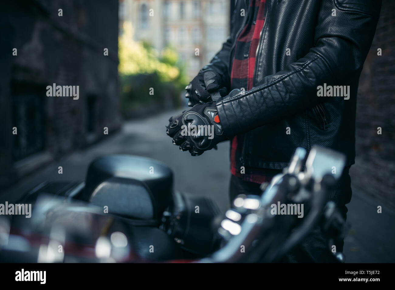 Male biker in leather jacket puts on gloves before riding on classical ...