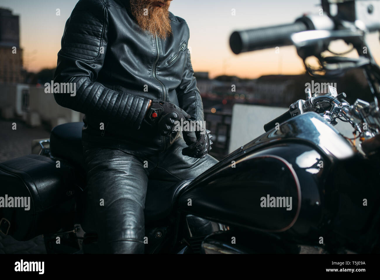 Biker poses on a motorcycle in city on sunset, classical chopper ...