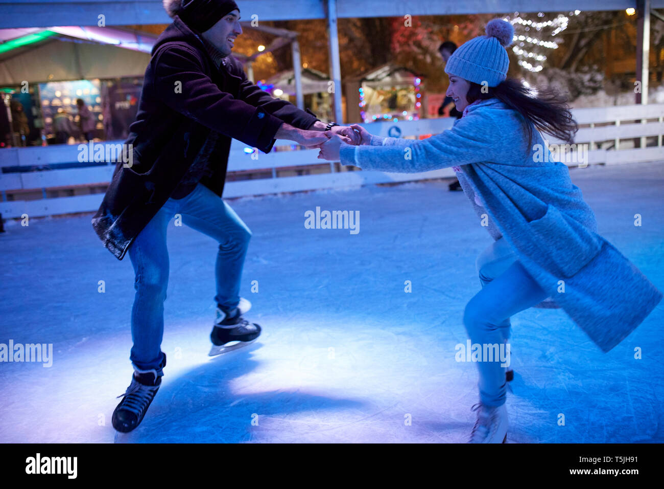 Happy young couple ice skating on an ice rink at night Stock Photo - Alamy
