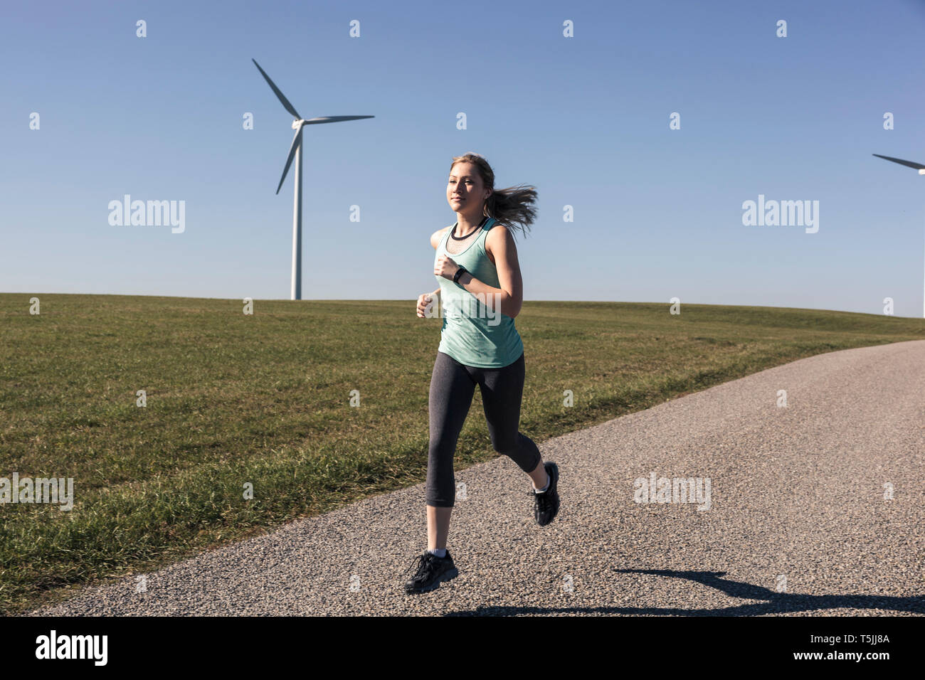 Young woman jogging on field way, wind wheels in the background Stock ...