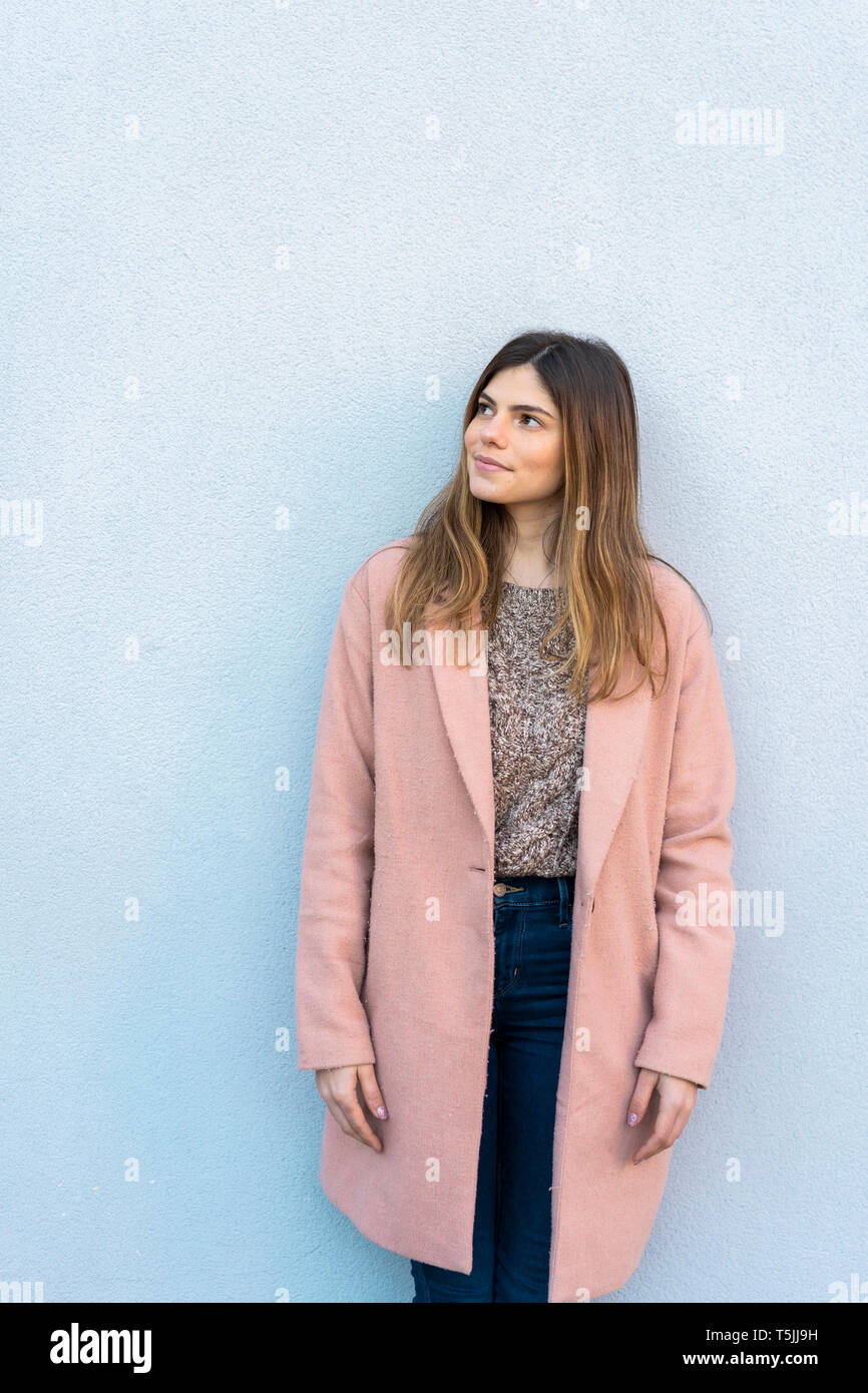 Young woman standing at a wall looking around Stock Photo - Alamy