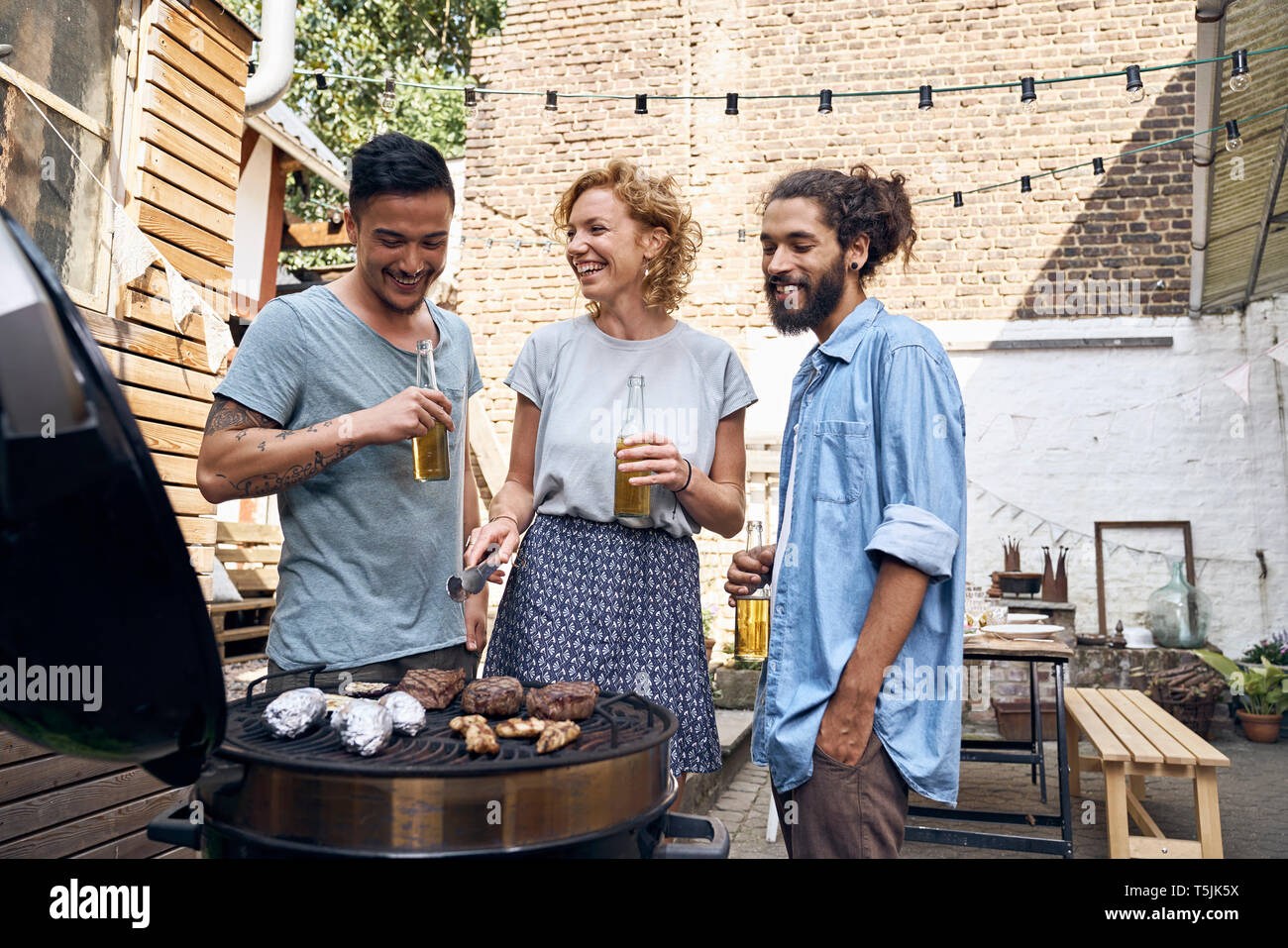 Friends having a barbecue n the backyard, preparing meat on a grill ...