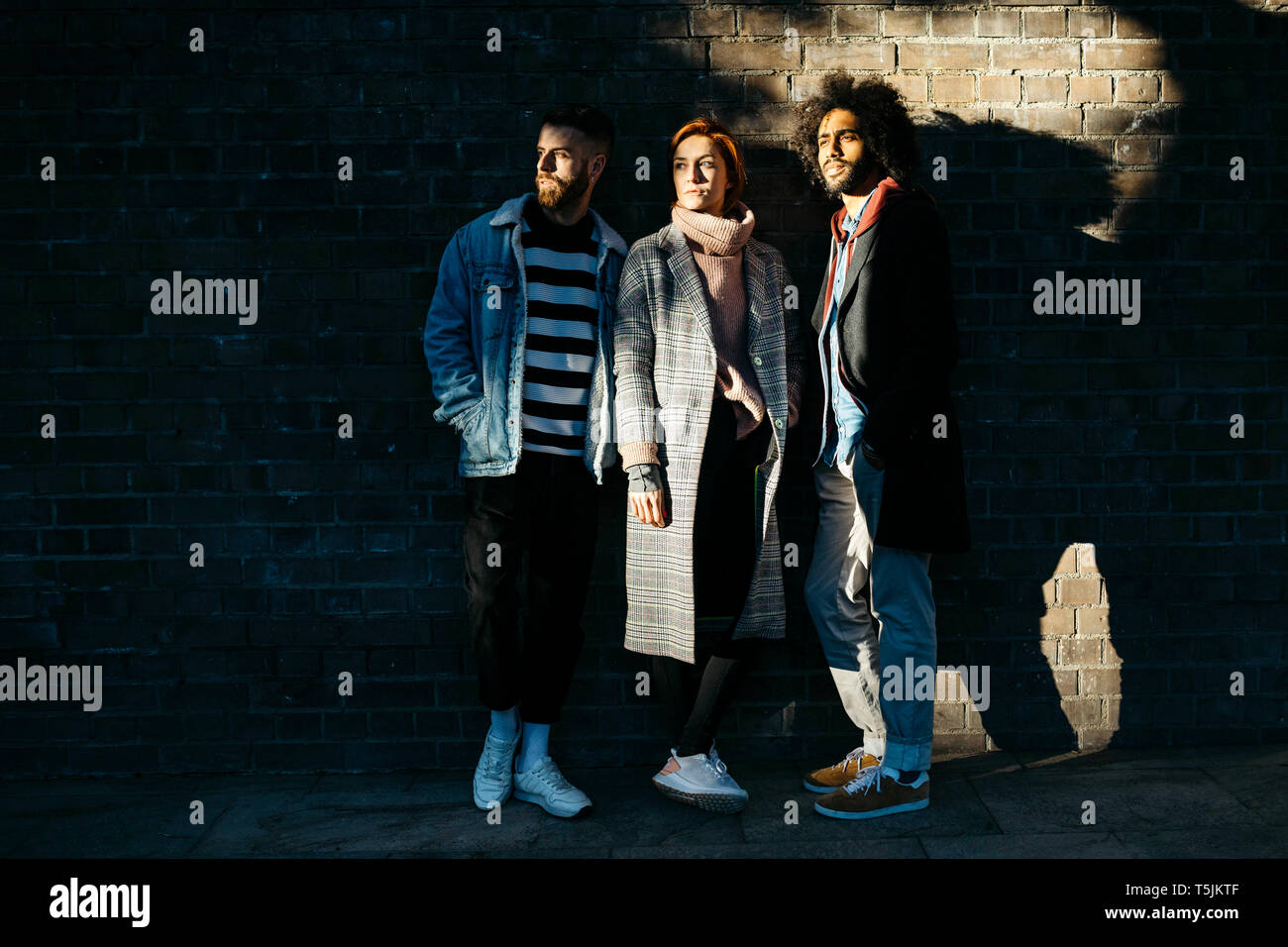 Three serious friends standing at a brick wall in shadow Stock Photo ...