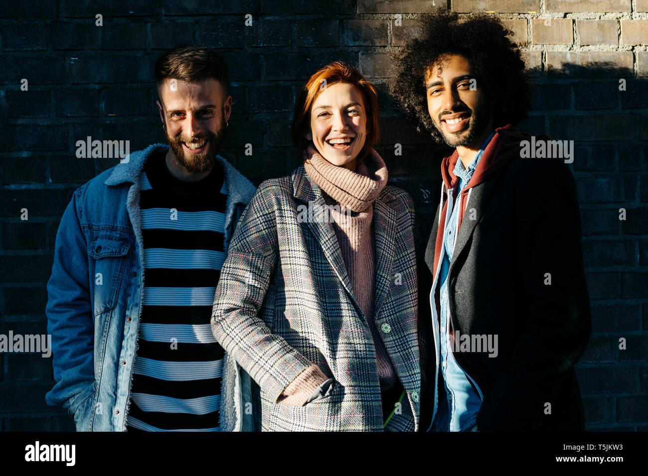 Portrait of three happy friends in shadow at a brick wall Stock Photo ...