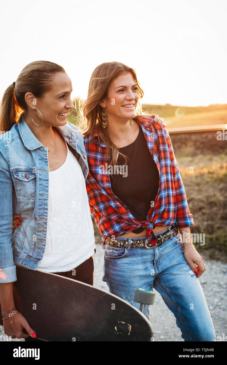 Two smiling friends with longboard at evening twilight Stock Photo - Alamy