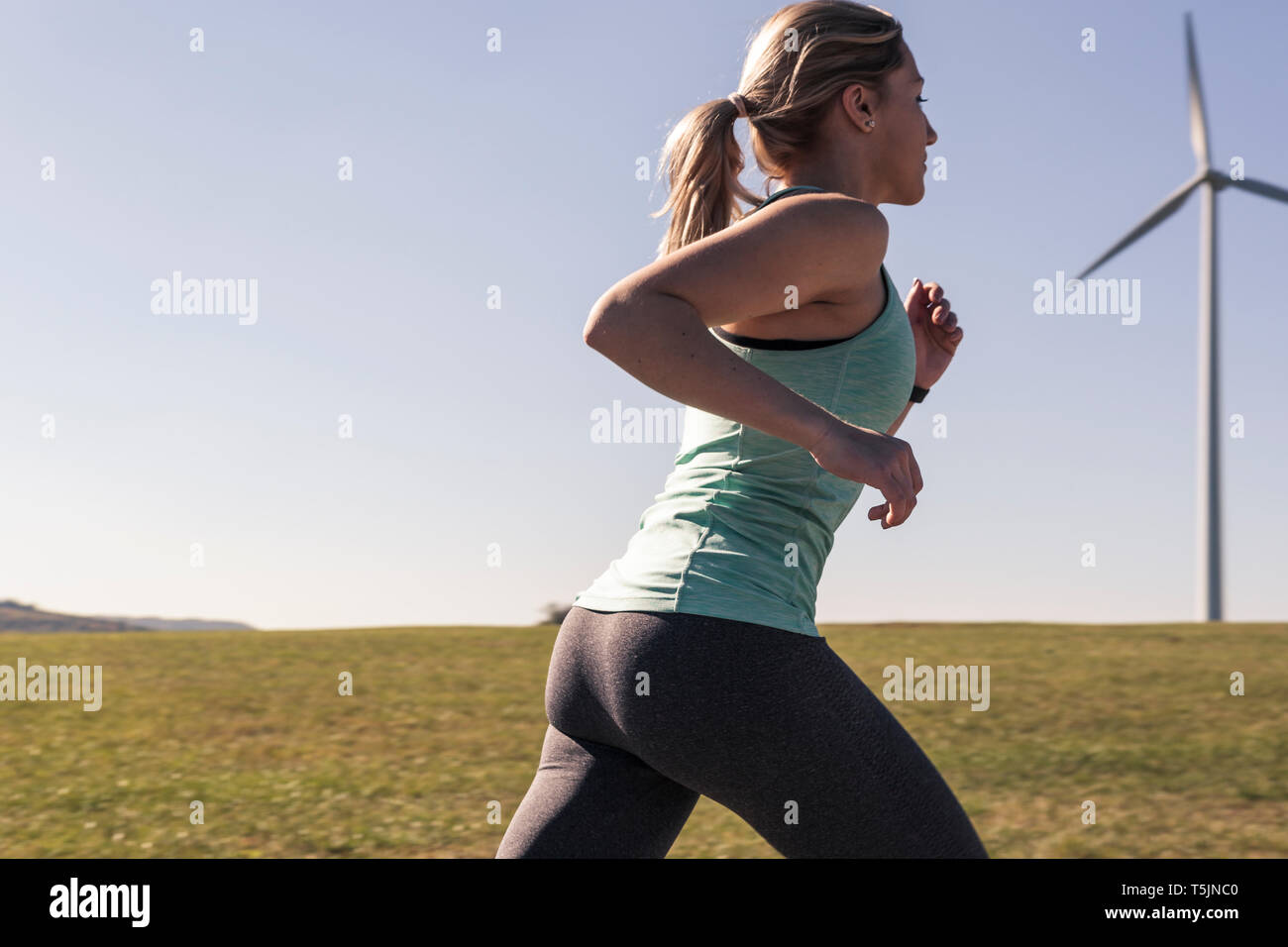 Young woman jogging on field way, wind wheels in the background Stock ...