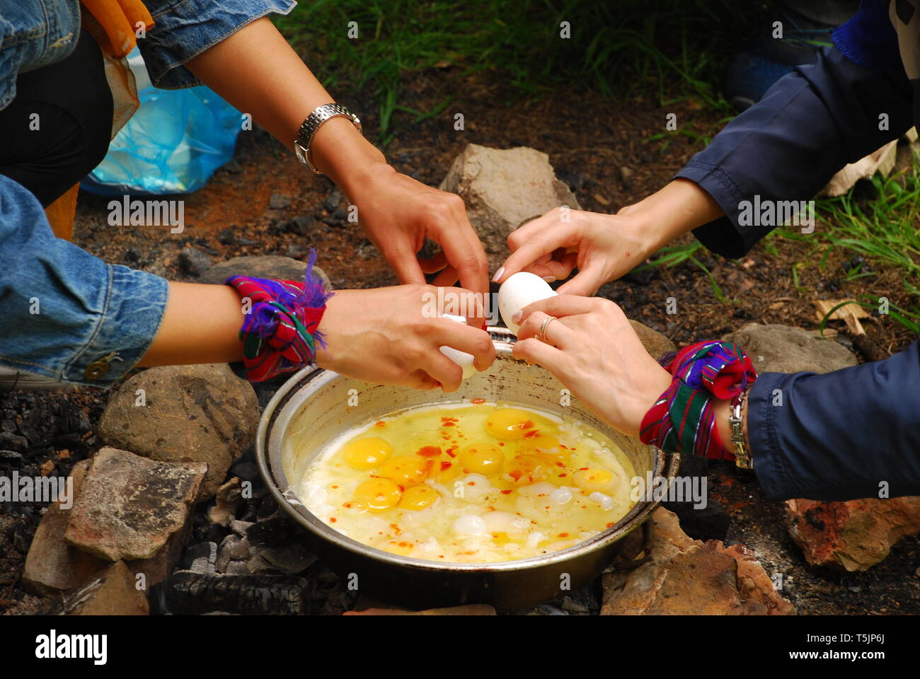 two girls cooking sunny side up eggs over charcoal fire in iron frying ...
