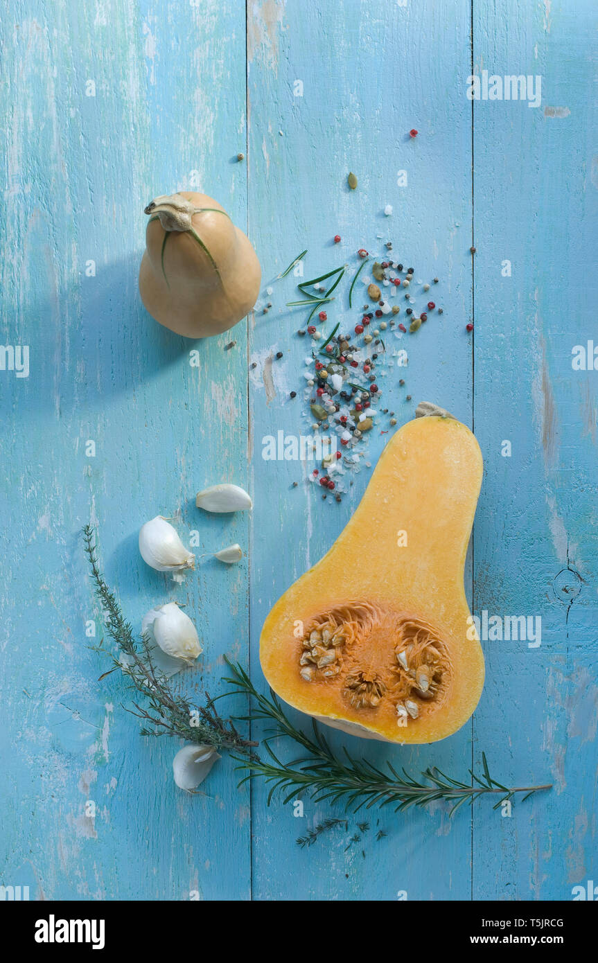 Whole and sliced butternut squash, garlic cloves and herbs on light ...