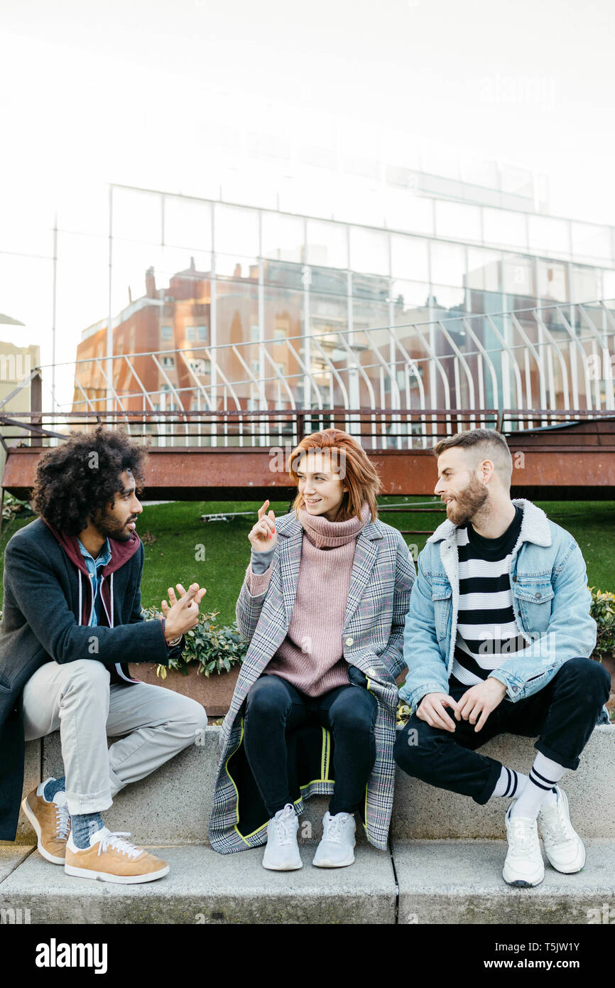 Three friends sitting in the city talking Stock Photo - Alamy