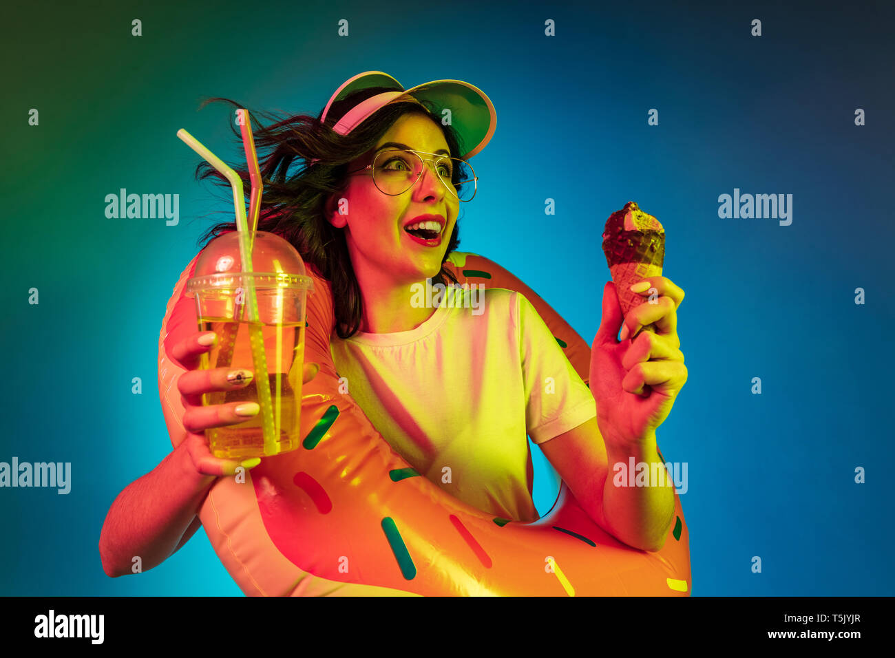 Happy young woman in a rubber ring with an icecream and drink on trendy ...