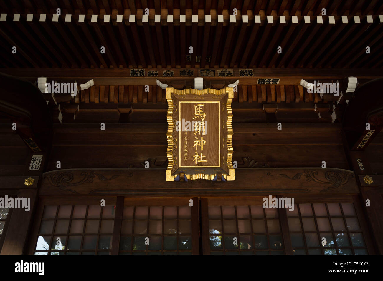 A gold plaque sign written "Maginu Shrine" hangs above main entrance of ...