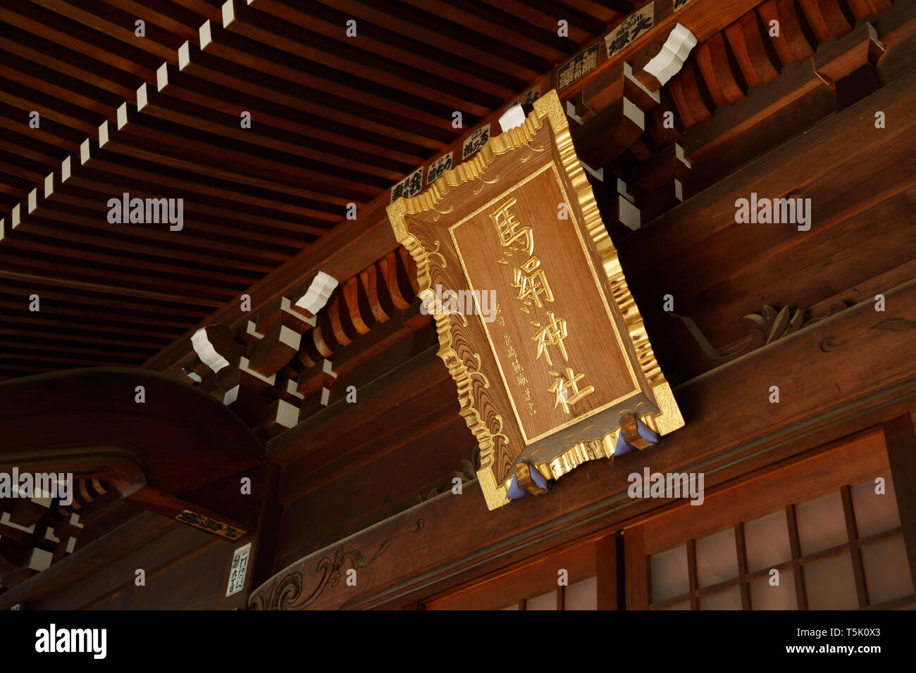 A gold plaque sign written "Maginu Shrine" hangs above main entrance of ...