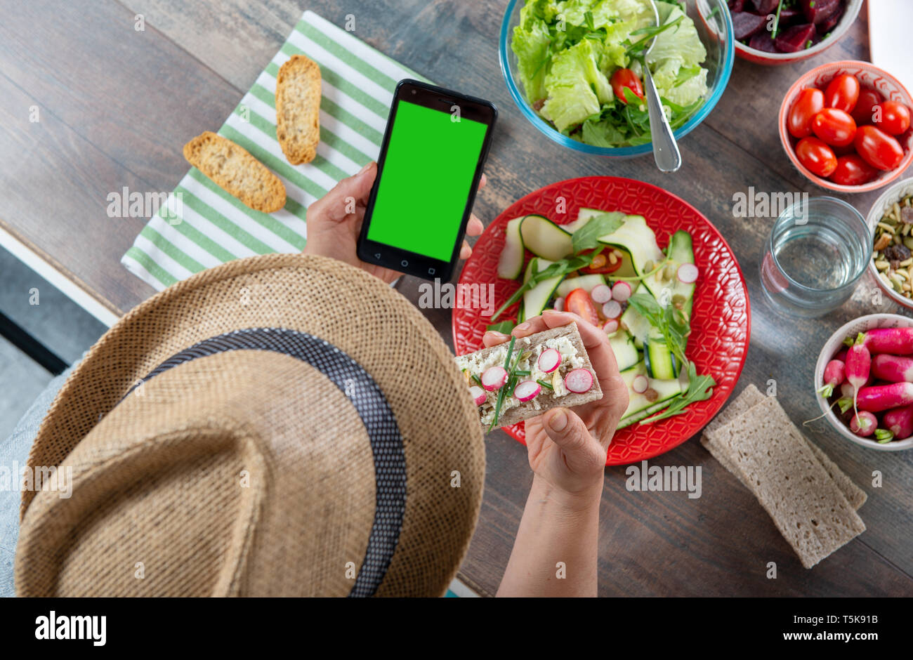 a woman eating a vegan salad and using a smartphone, green screen, top ...