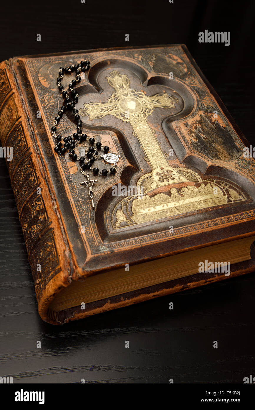 Ancient leather bound gilded Holy Bible with Rosary beads on black oak ...