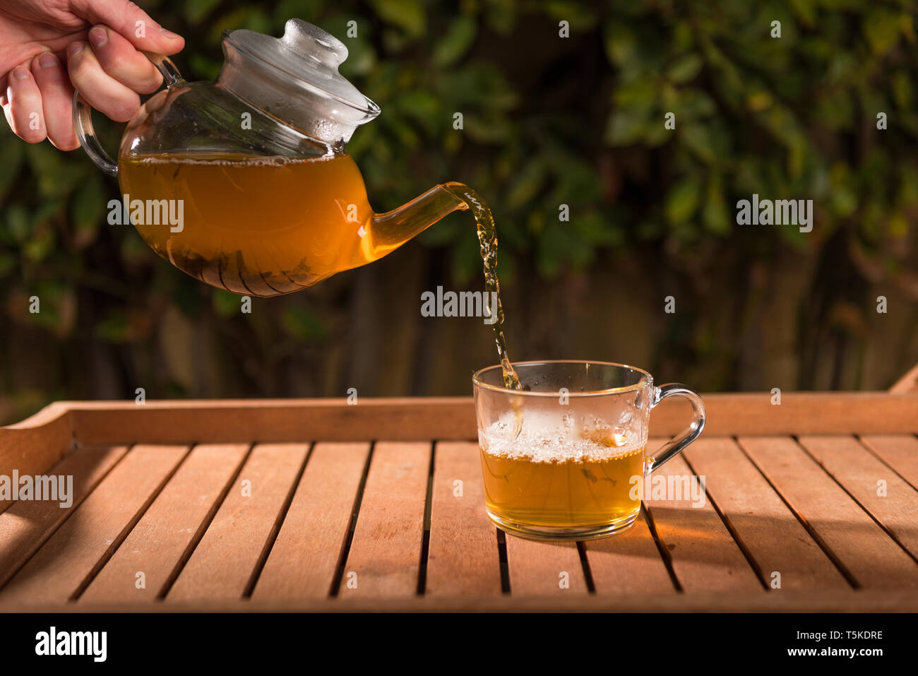 Pouring tea from teapot into a cup, natural background Stock Photo - Alamy