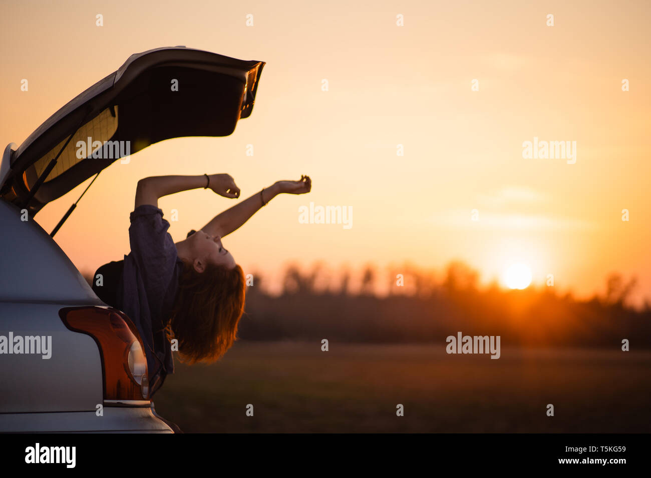 Beautiful young woman happy and dancing in a car's trunk during a road ...