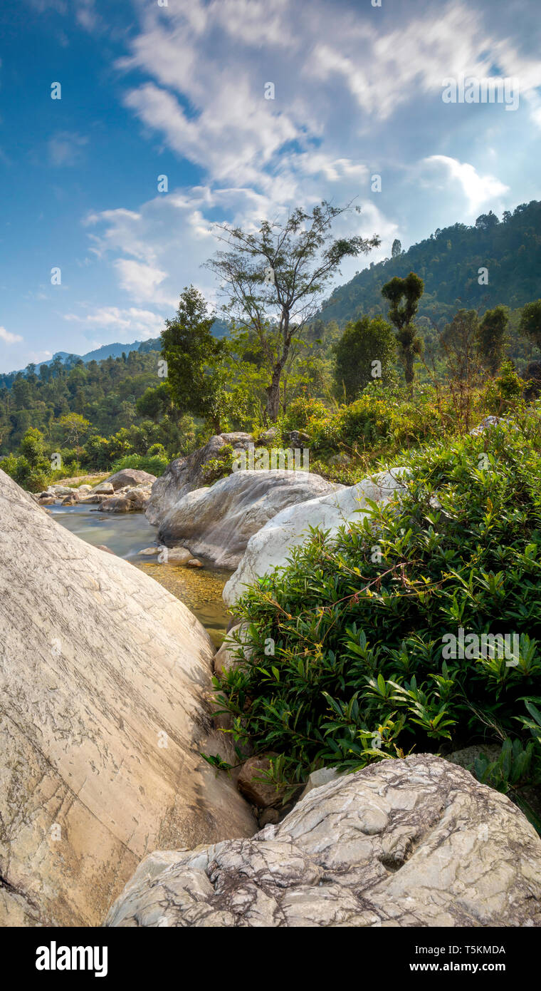 a small river side different size rocks and background hills blue sky ...