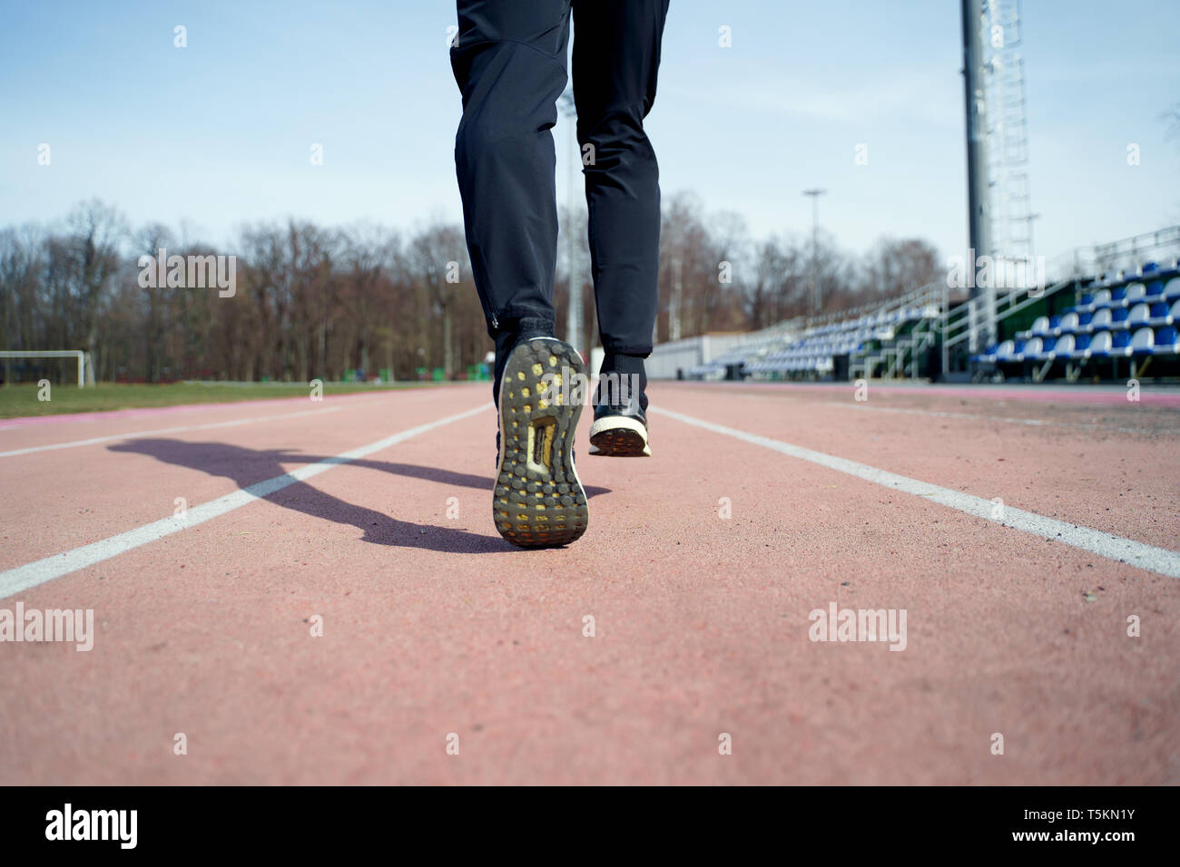 Photo from back of legs of athlete running through stadium on spring ...