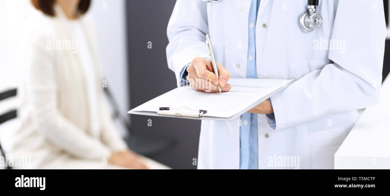 Doctor woman filling up medical form while standing near reception desk ...