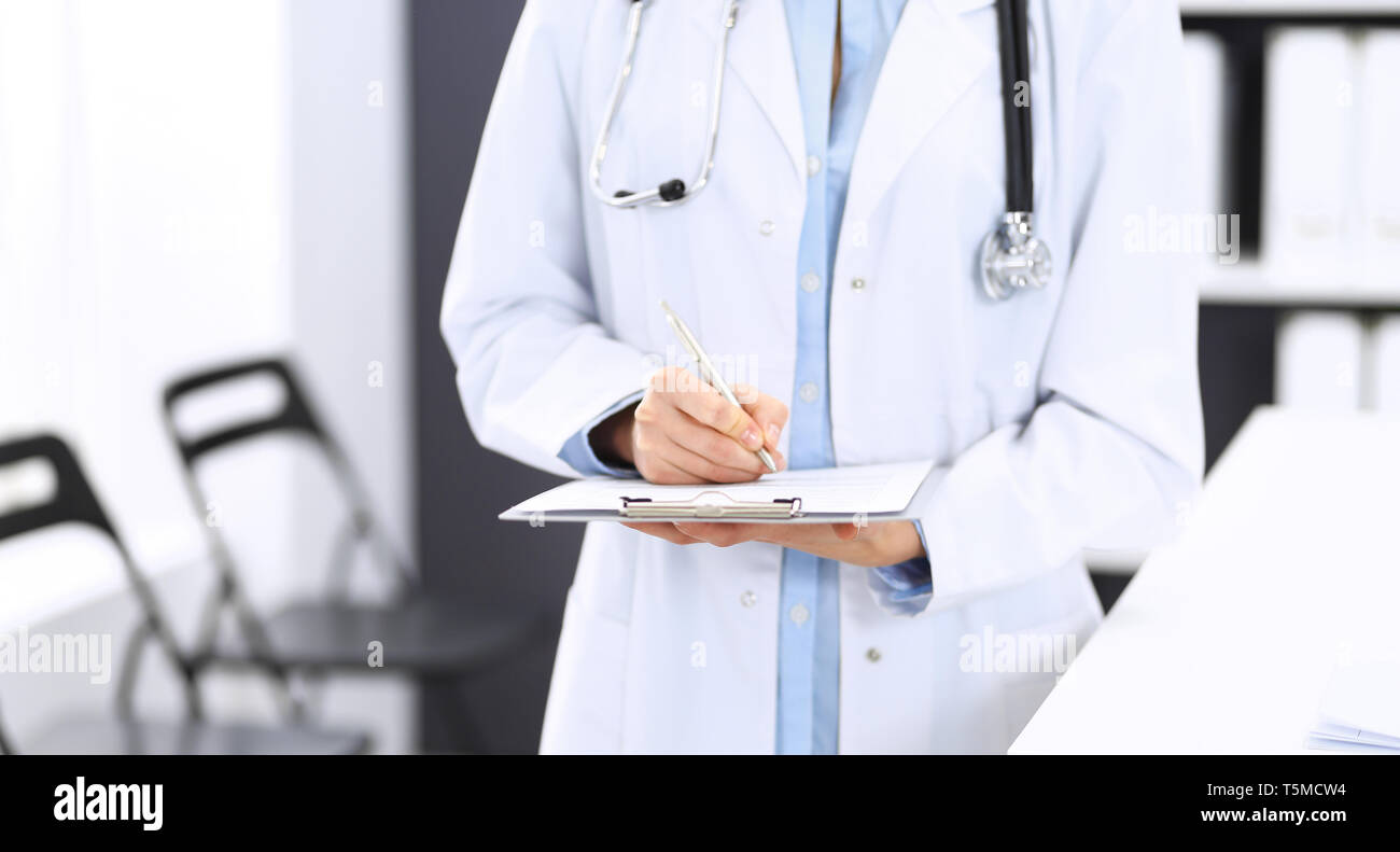 Doctor woman filling up medical form while standing near reception desk ...
