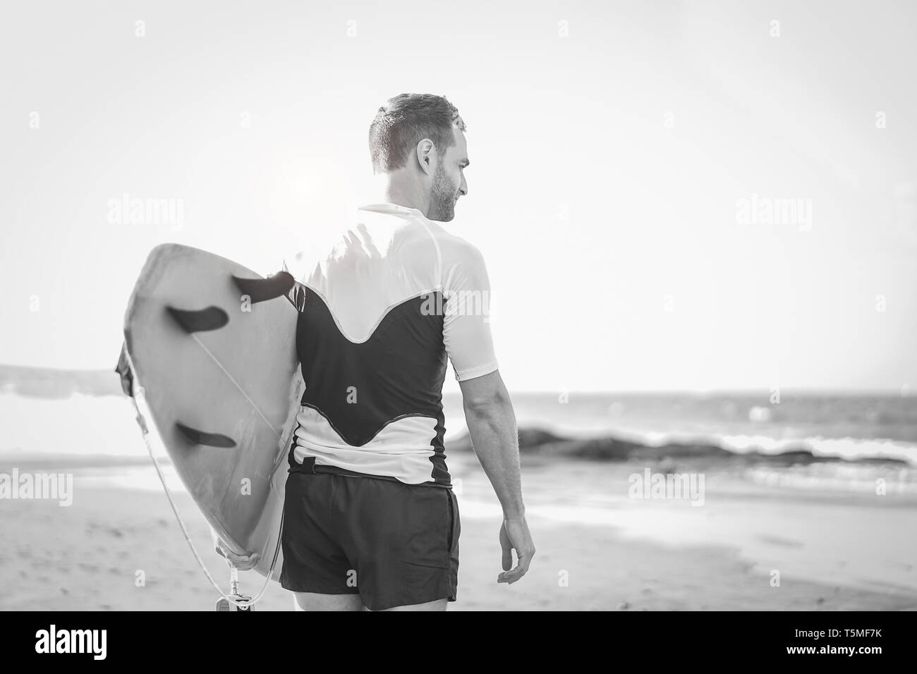 Young surfer holding his surfboard on the beach - Handsome man waiting ...