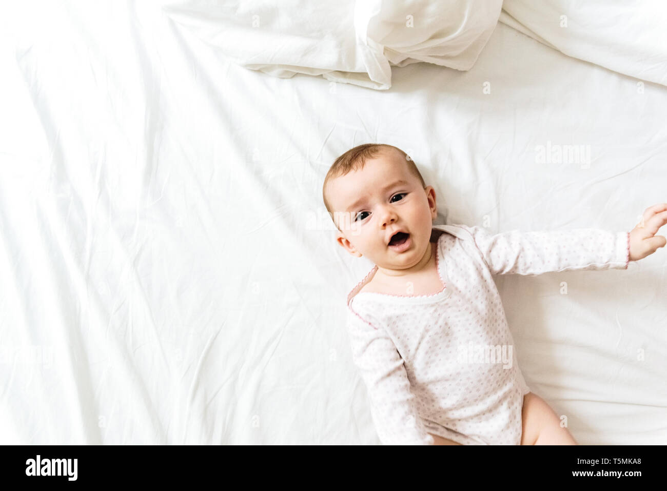 Happy and smiling adorable 6 month old baby girl lying on a bed ...
