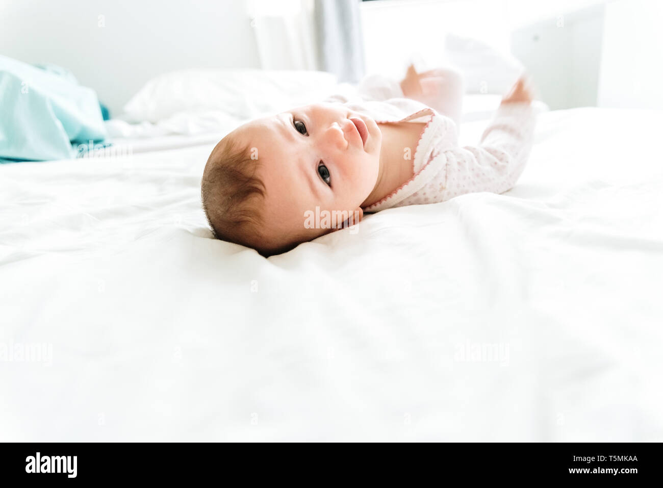 Happy and smiling adorable 6 month old baby girl lying on a bed, lifestyle isolated on natural ...