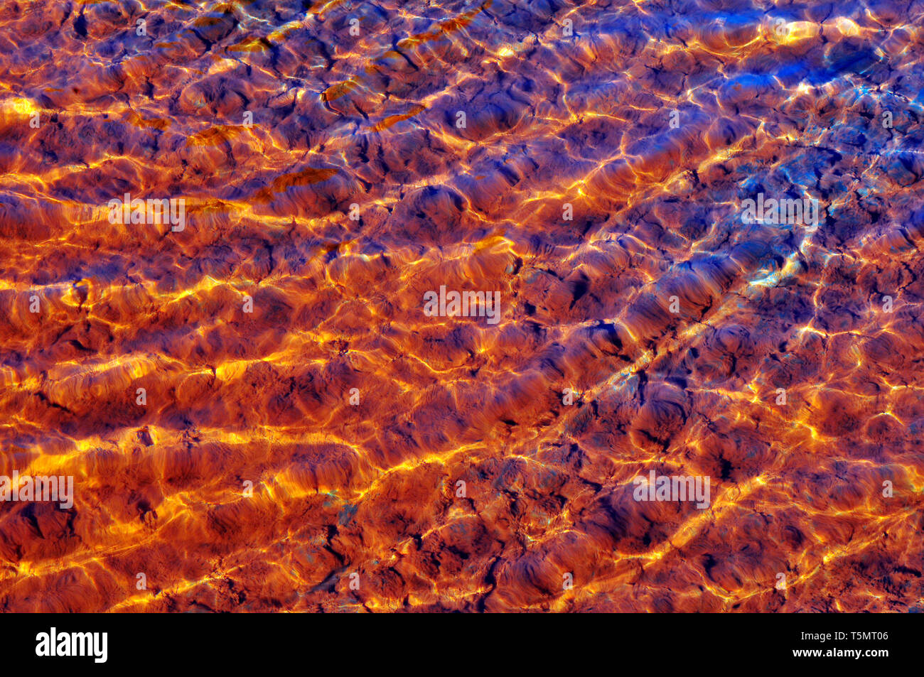 A close up of a stream with clear water running over a rust-red ...