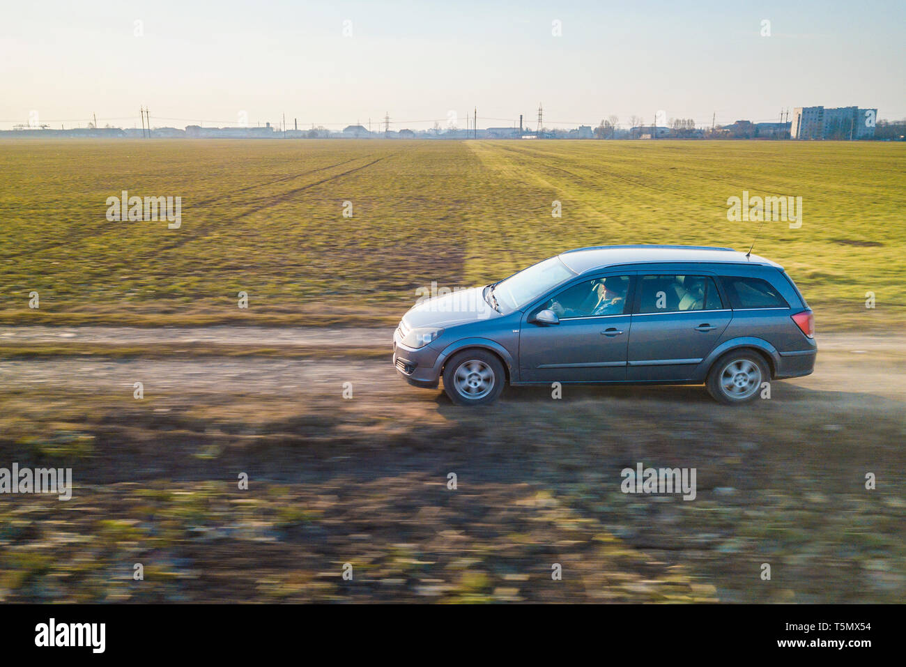 Aerial view of car driving by straight ground road through green fields ...