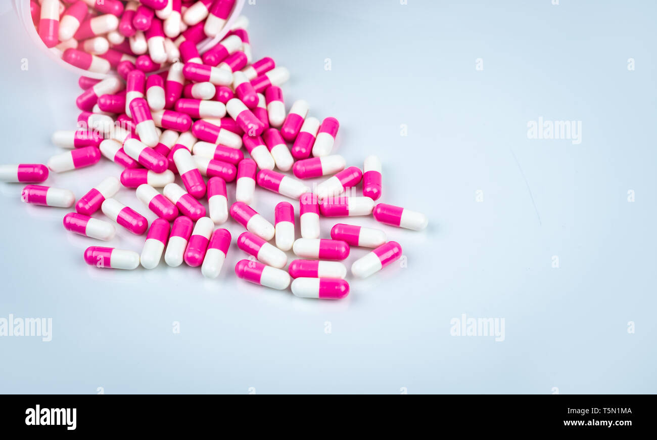 Pink and white capsules pill spilled out from white plastic bottle ...