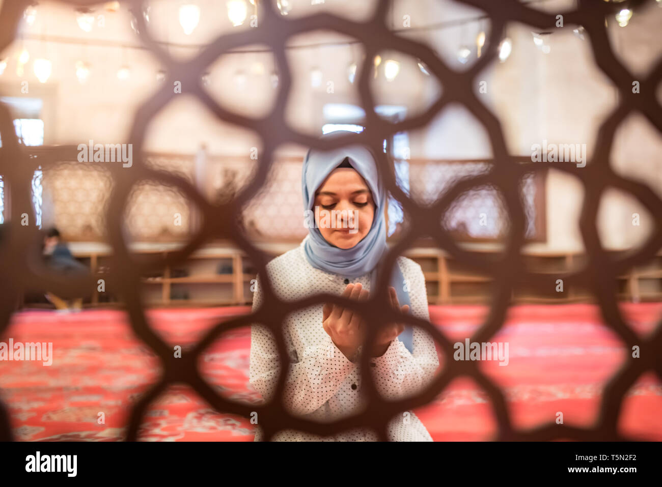 View through fence:Muslim woman in headscarf and hijab prays with her ...