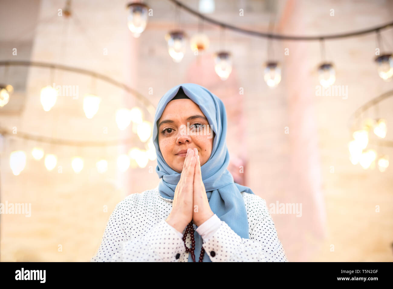 Muslim woman in headscarf and hijab prays while clasping her hands with ...