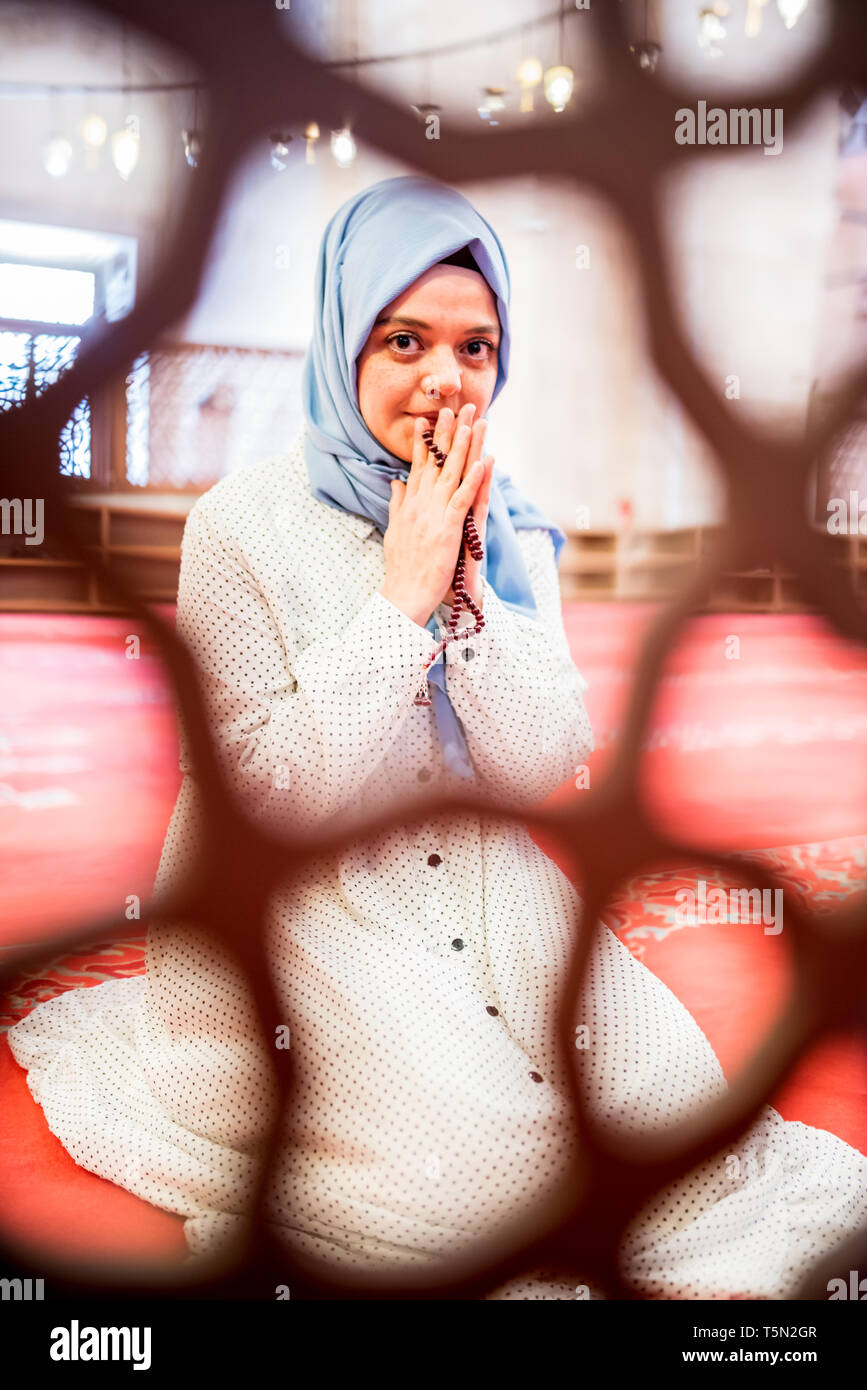 Muslim woman in headscarf and hijab prays while clasping her hands with ...