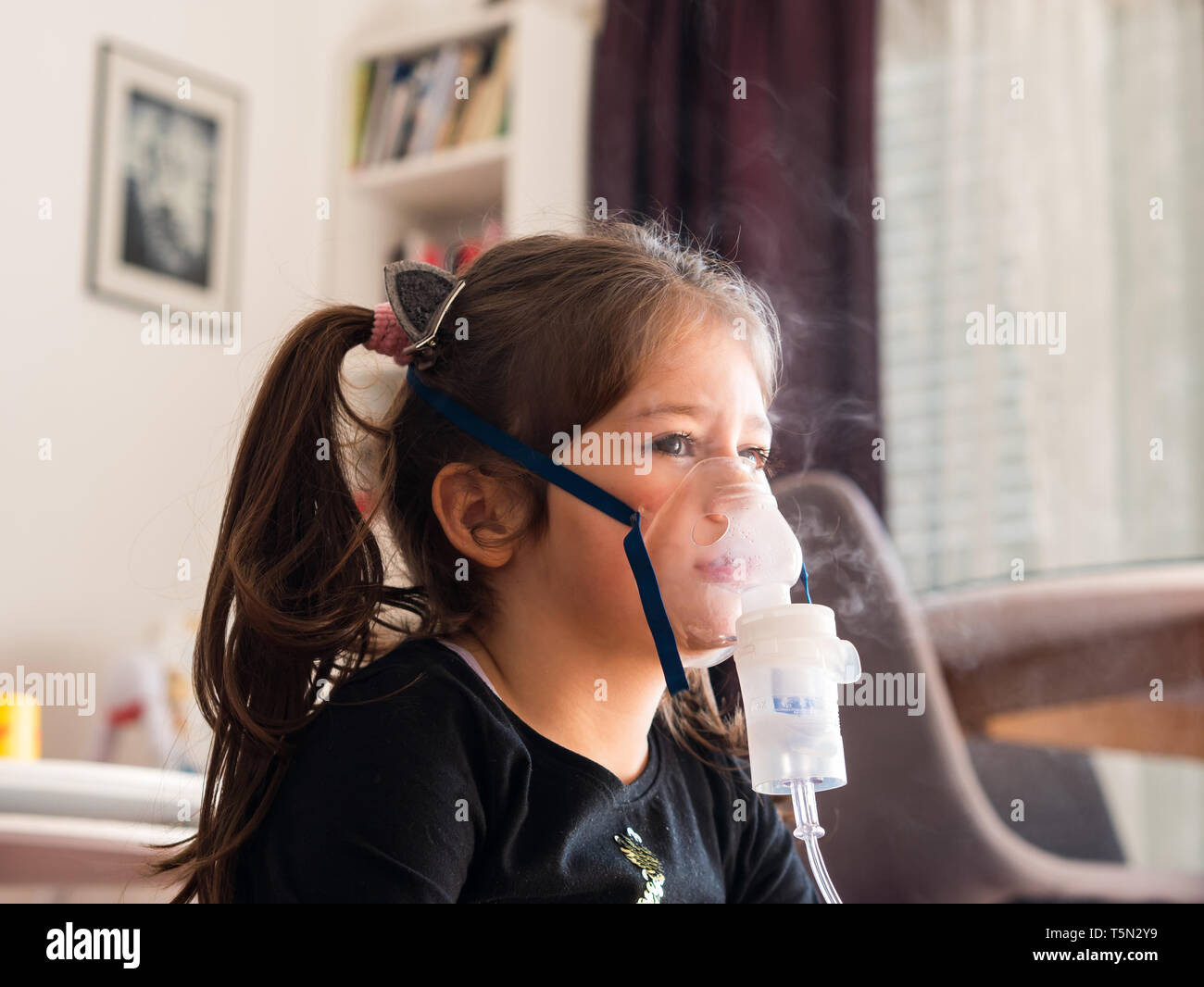 Adorable caucasian girl sitting at home and inhaling with oxygen mask ...
