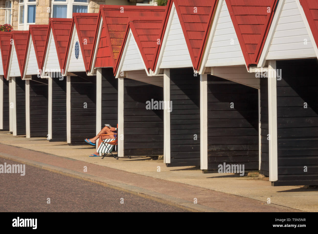 Beach huts on Bouremouth sea front, with loan sunbather sitting in ...