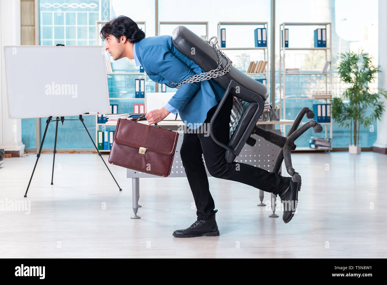 Chained male employee unhappy with excessive work Stock Photo - Alamy