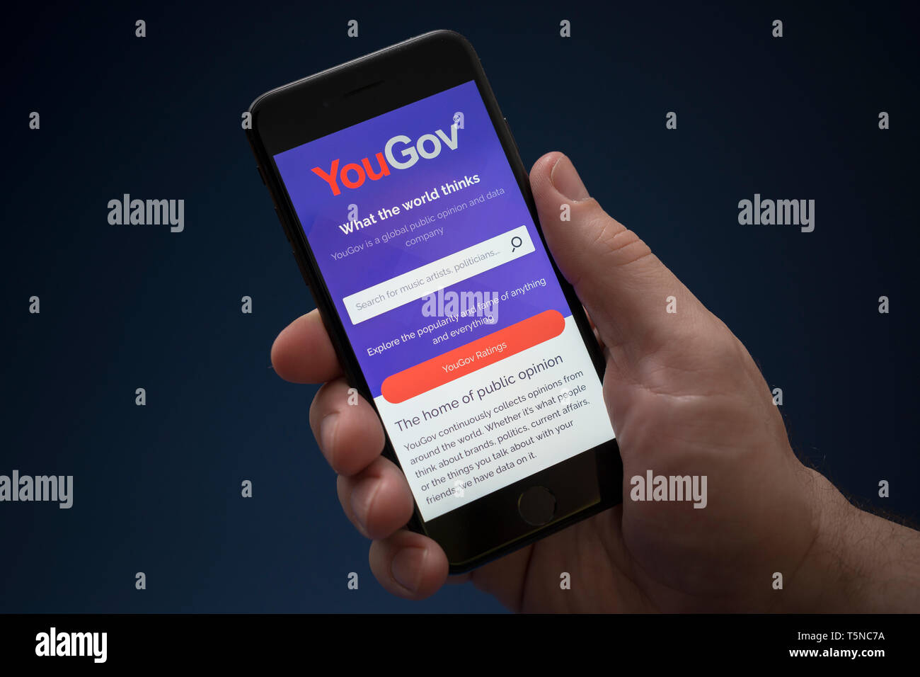 A man looks at his iPhone which displays the YouGov logo (Editorial use ...